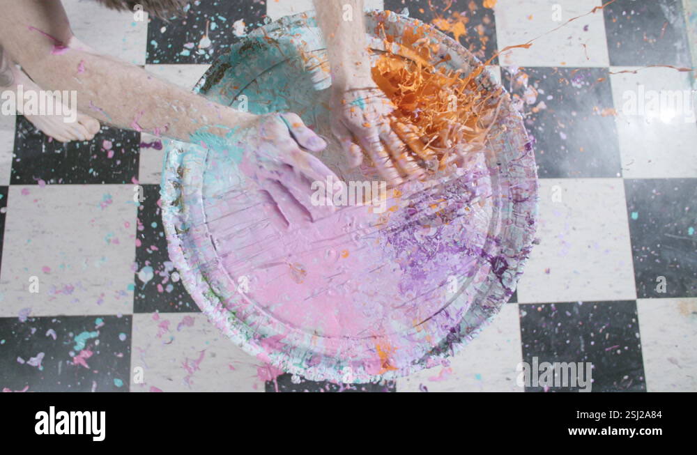 Man smacking on a drum that is filled with different colored paints and ...