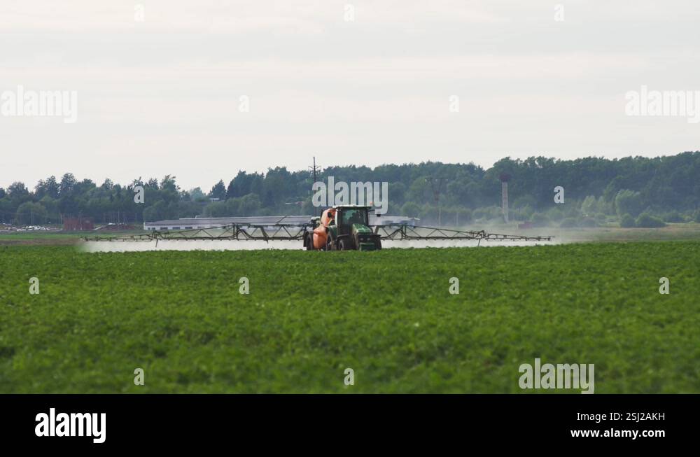 Tractor with fertilizer spreading equipment spraying on green field ...