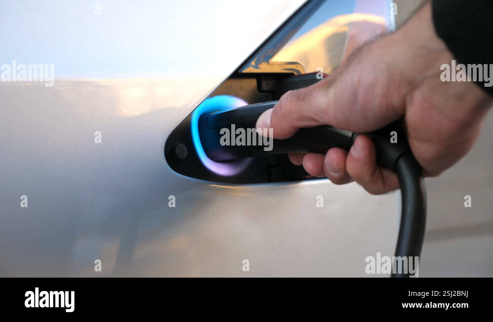 Hand opening an electric car charging socket cap and plugging in a ...