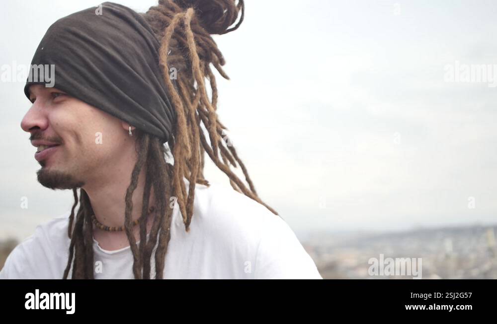 A young attractive guy with a charming smile and dreadlocks wears beads ...
