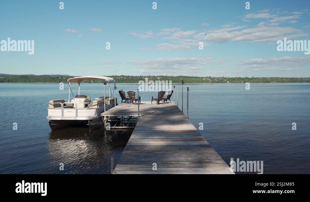 Walking down a dock with muskoka chairs and a boat docked revealing the ...