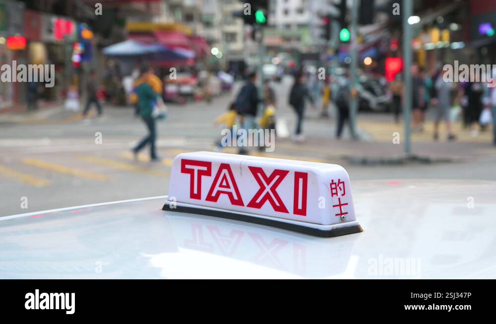 A taxi sign sits on the hood of the vehicle as pedestrians and traffic ...