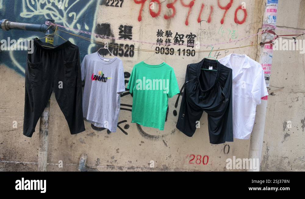 Outdoor street laundry hanging from pipes next to a wall with graffiti ...