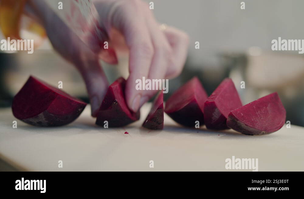 A woman chef carefully and expertly cuts vibrant beetroot into sectors ...