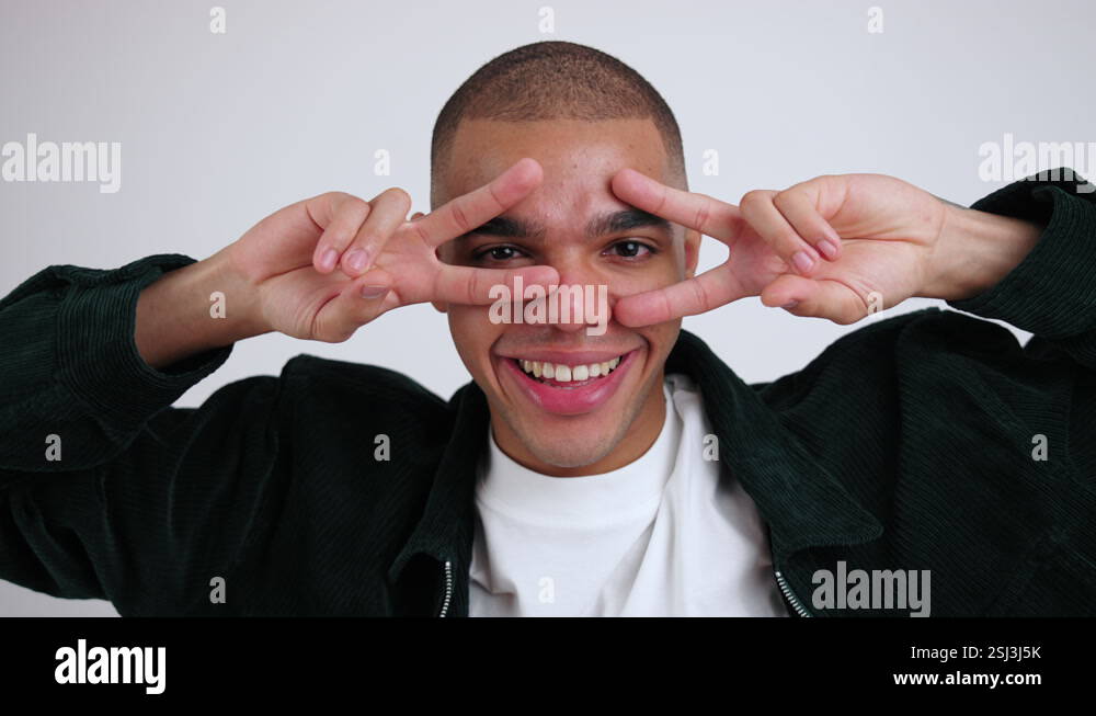 Crazy funny young adult man doing v sign in front of his face with both ...