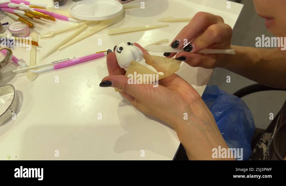 Woman hands up close shaping white fondant dog with a spatula, zoom out ...