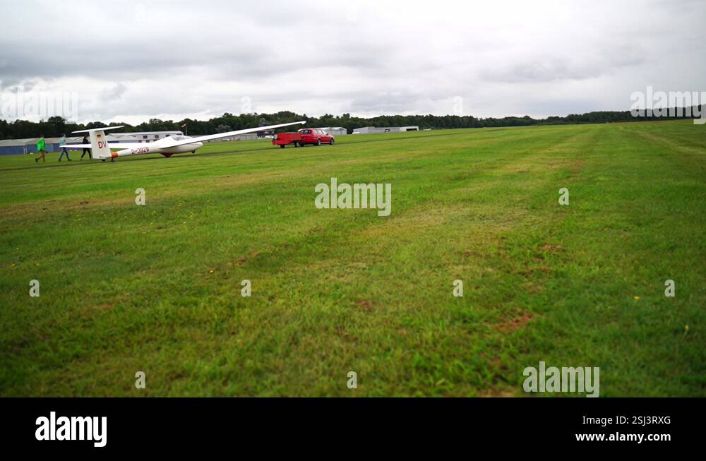 small plane is pulled by a red car over an airfield with a meadow Stock ...