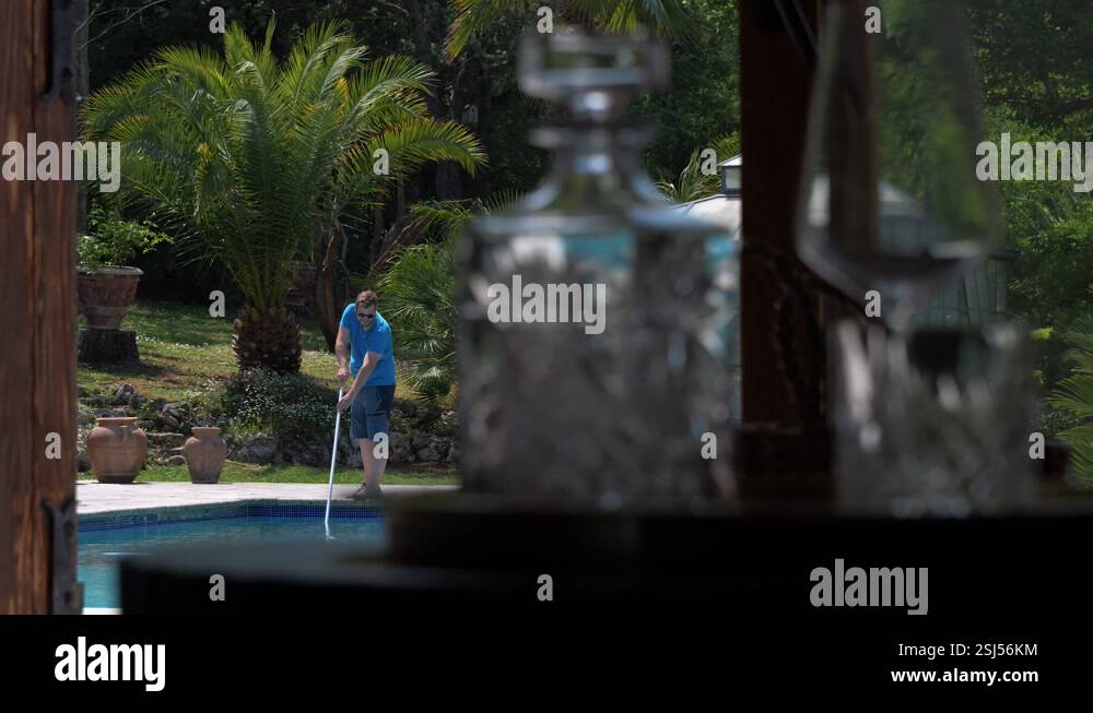 a swimming pool operator seen behind a glass bottle, cleaning a pool ...
