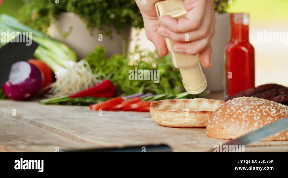 Close up hands drizzle dressing sauce onto toasted burger bun preparing ...