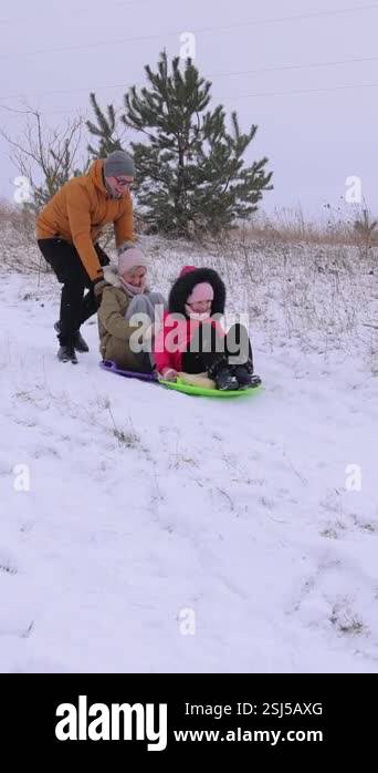 Vertical video. A snow slide where a family is having fun on plastic ...