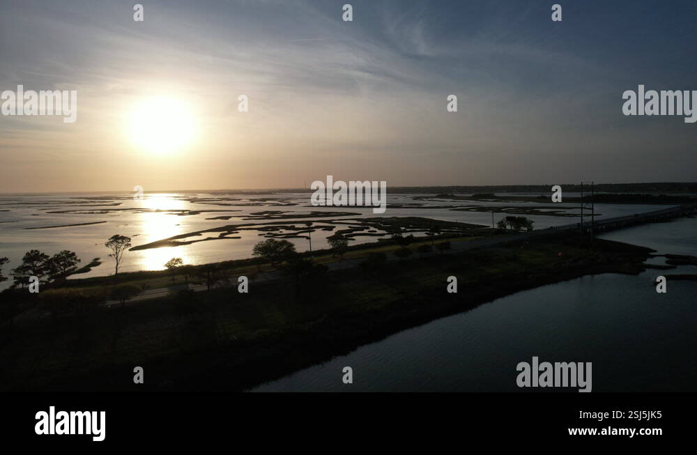Sunsetting over salt marsh with cars coming across a bridge, Emerald ...