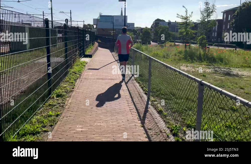 Running male trail runner followed along train tracks on walk path over ...