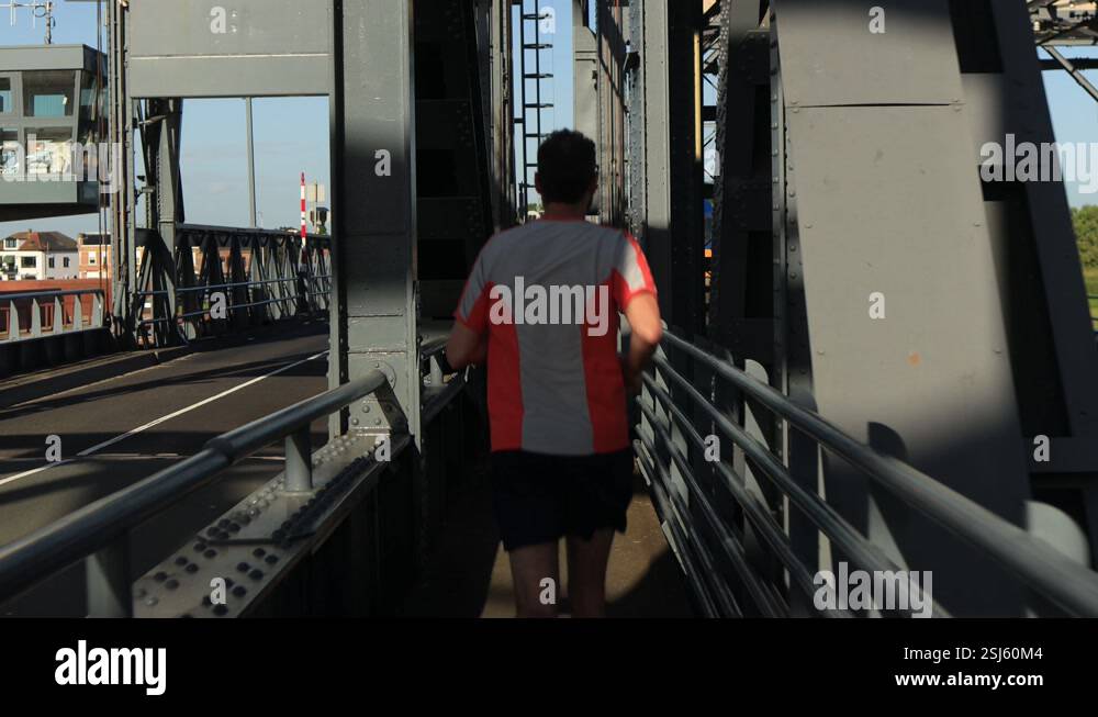 Seen from behind middle aged male trail runner on steel bridge between ...