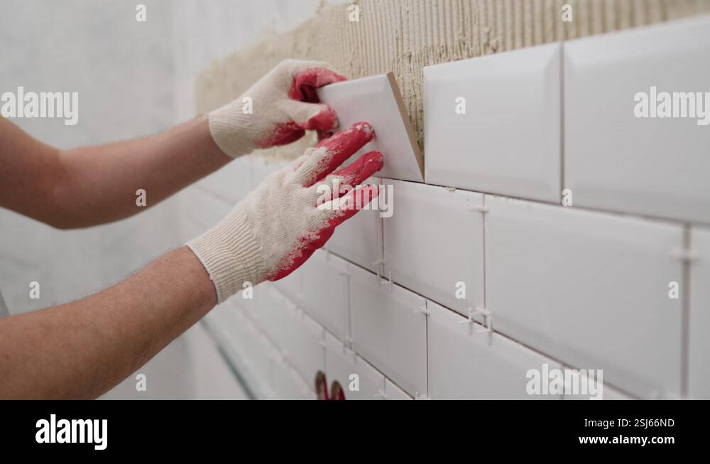 Tiler hands in the process of laying white rectangular tiles on ...