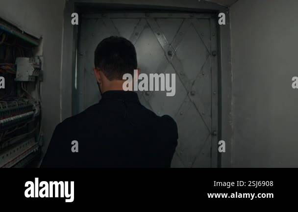 Back view of young priest wearing black cassock opening metal door and ...