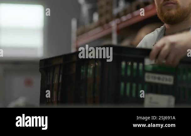 Male loader working in storage, placing crates with goods onto shelves ...