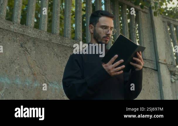 Low angle view of serious young priest wearing glasses and black ...