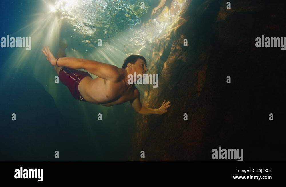 Man dives in the freshwater river with sunny rays shining through the ...
