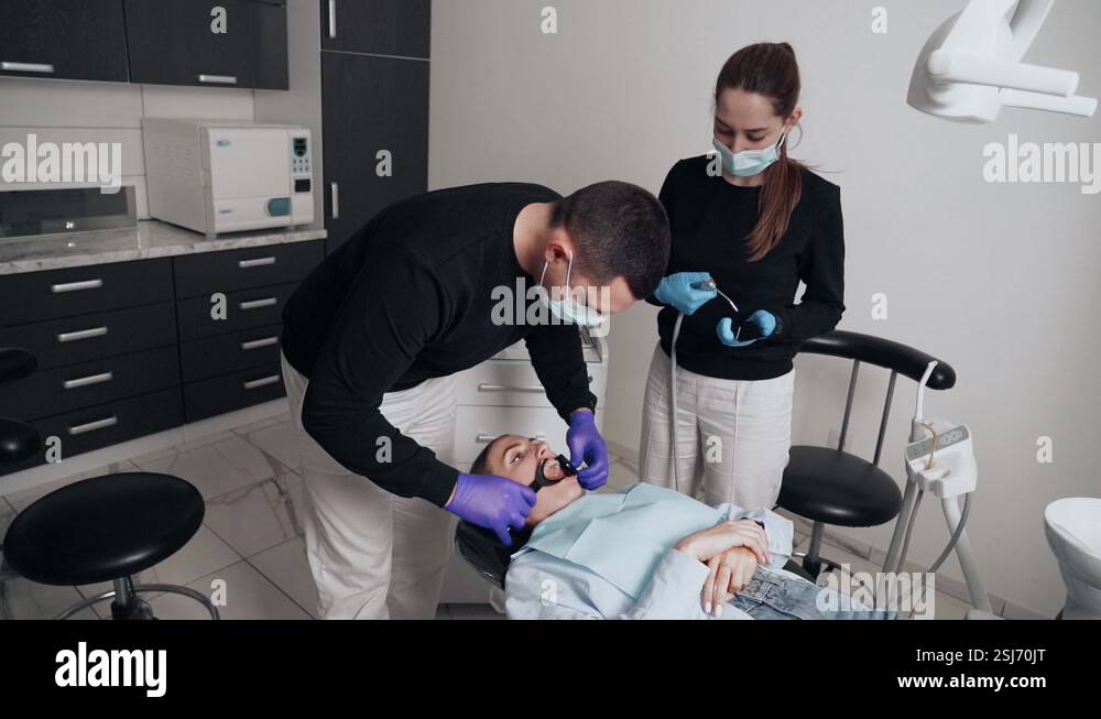 male dentist with face mask examining teeth of female patient at modern ...