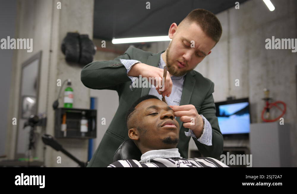Barber is shaving aligning hair of afroamerican man on forehead using ...