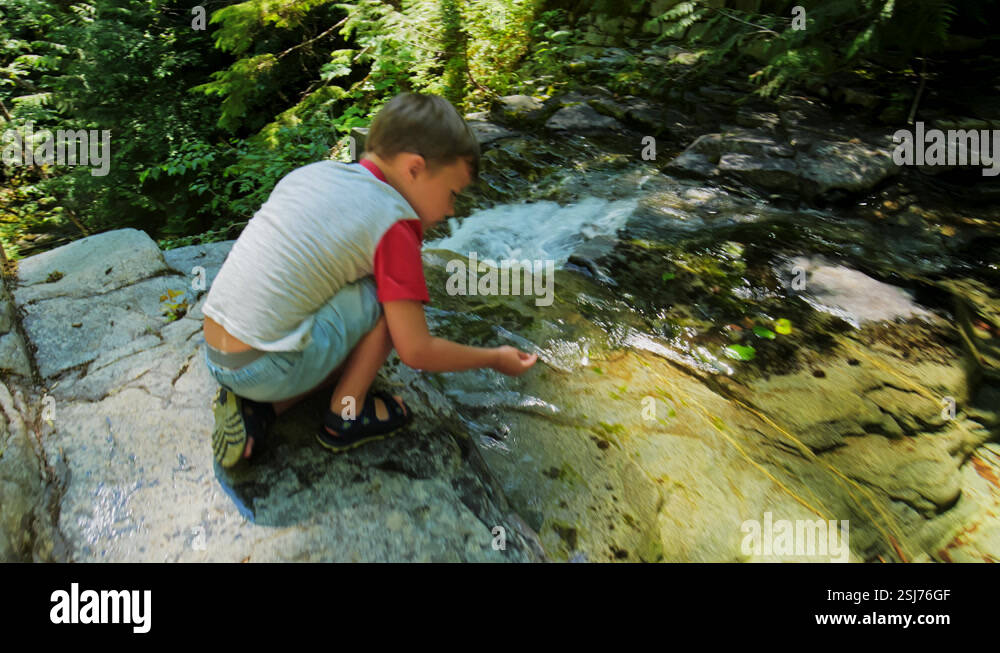Young Boy Kid Crouched Down Next to Waterfall on Top of Rocky Cliff in ...
