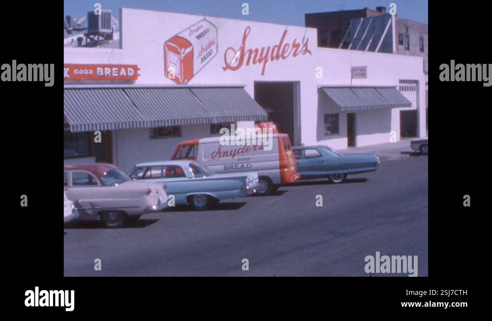 1960s: Cars parked outside of factory, van exits factory. Hand holding ...