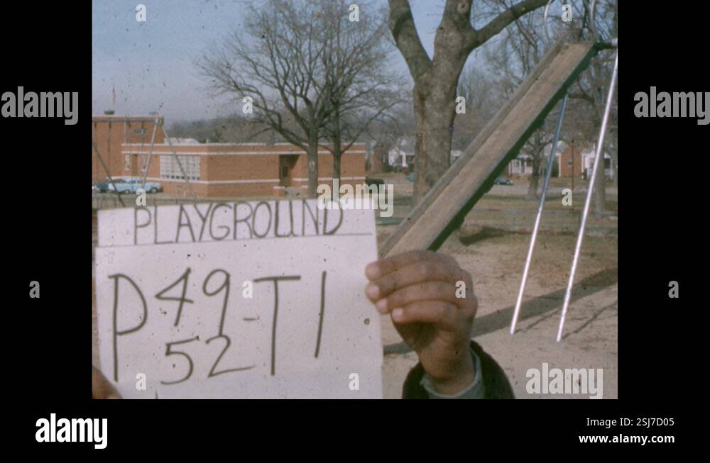 1960s: Playground, school building, cars. Boy slides down slide, sits ...