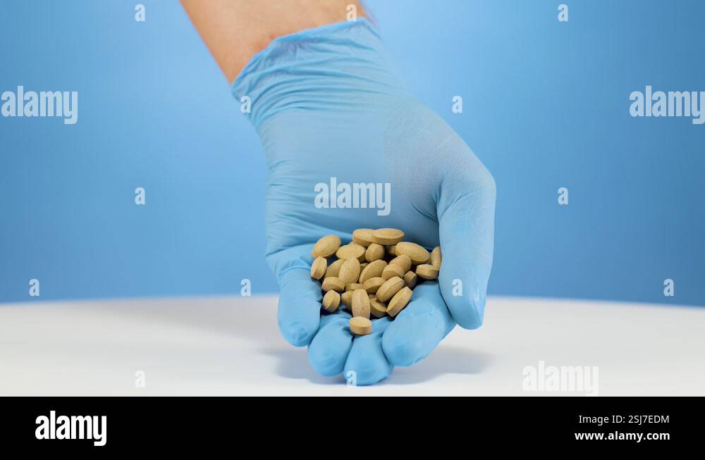 Hand with blue gloves shows handful of painkiller tablets with blue ...