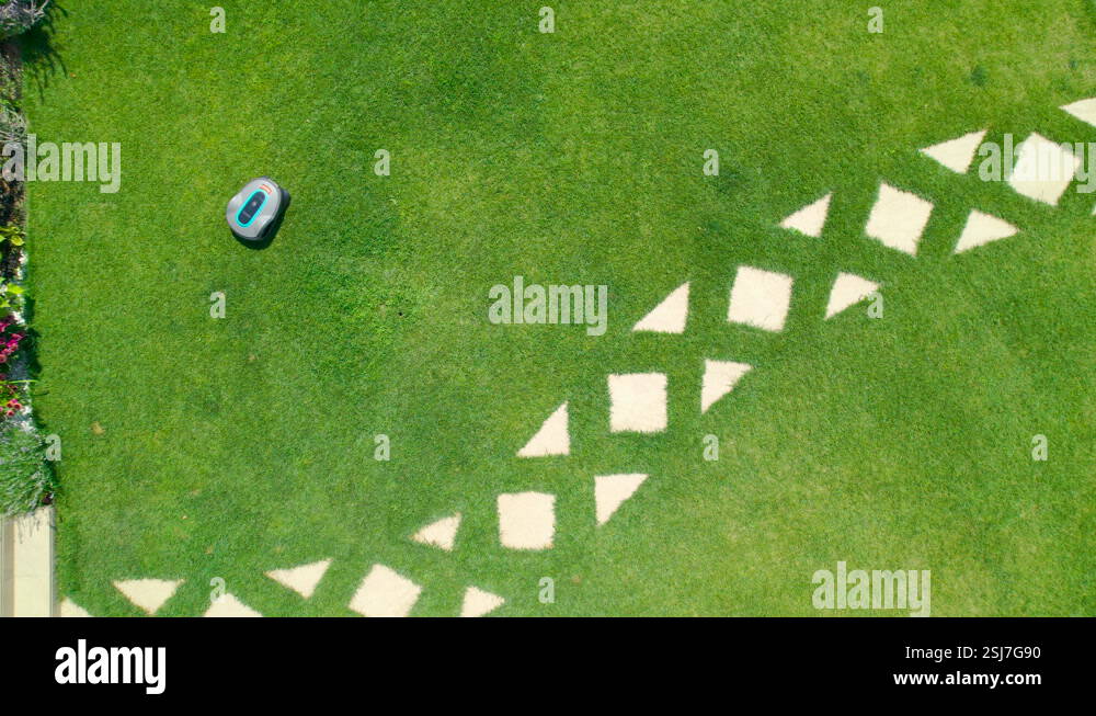 AERIAL TOP DOWN: Robotic lawn mower trimming green grass in well-kept ...
