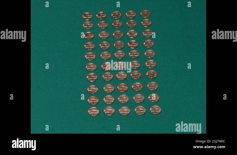 1960s: Fifty pennies sit on tabletop. Six marbles sit on tabletop. Hand ...