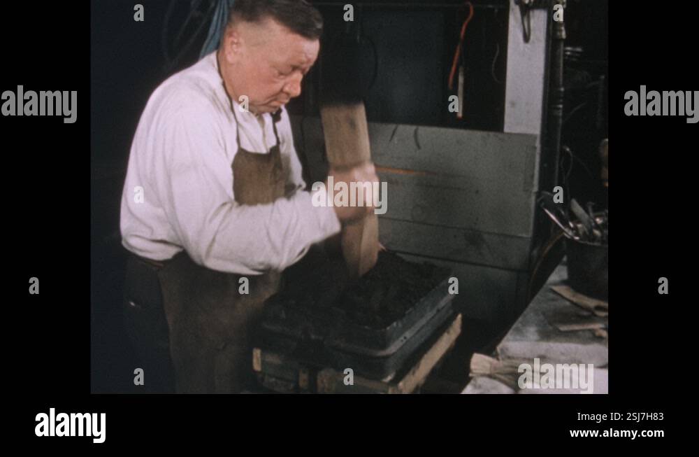 1950s: Workshop, man uses large wooden tamper to pack material into ...
