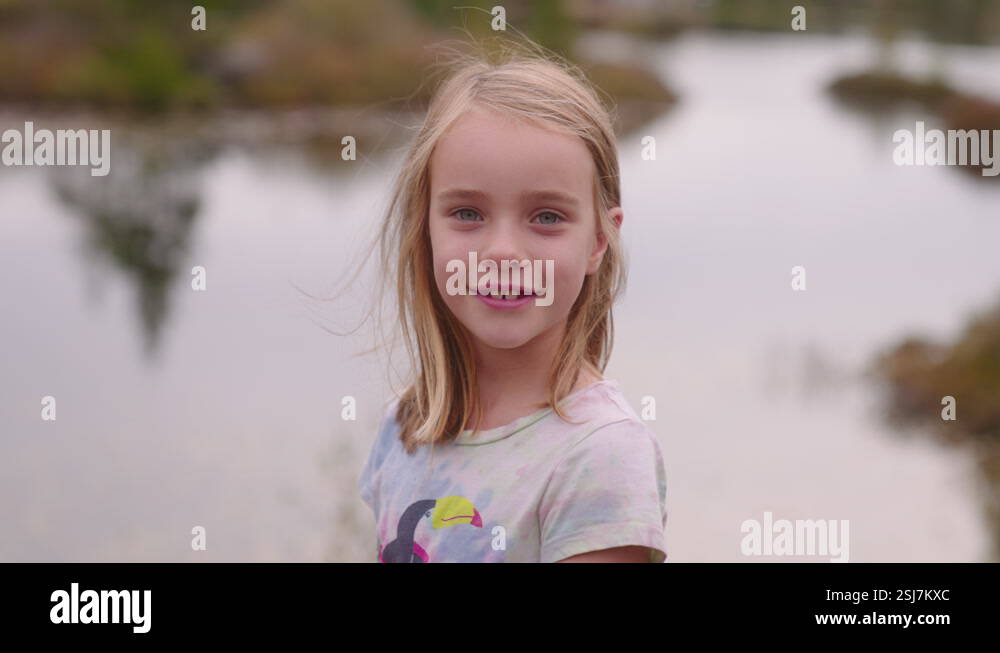 Pretty little girl looks out at a lake and turns around and smiles at ...