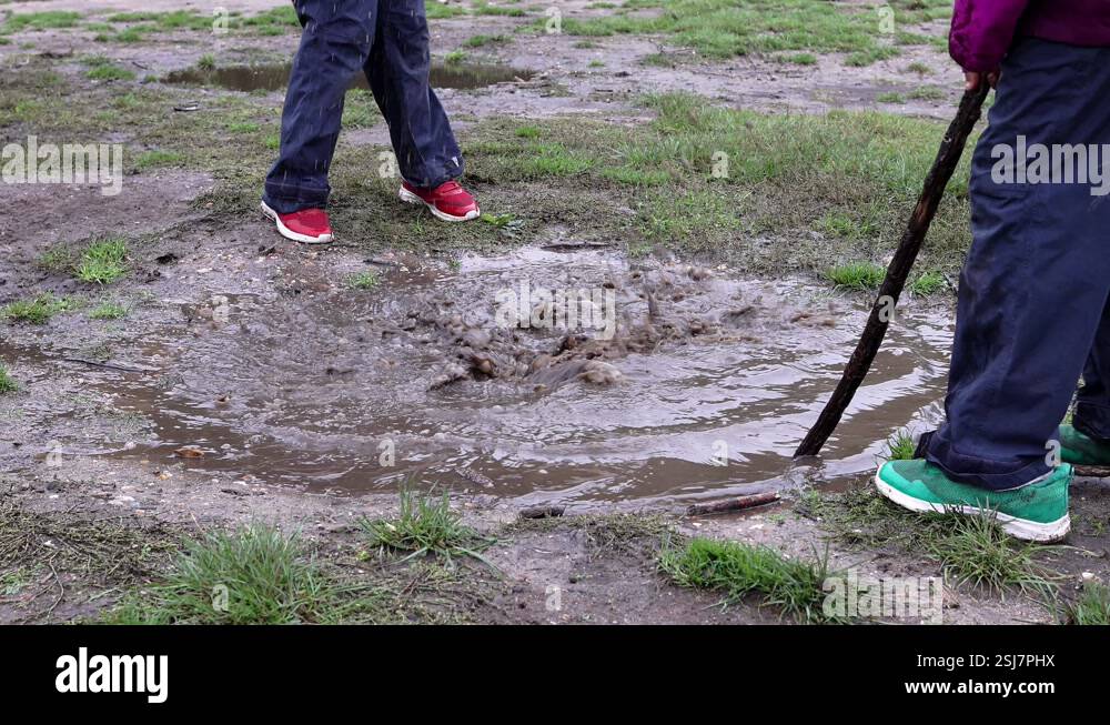 Two ethnically diverse children playing with sticks in a muddy puddle ...