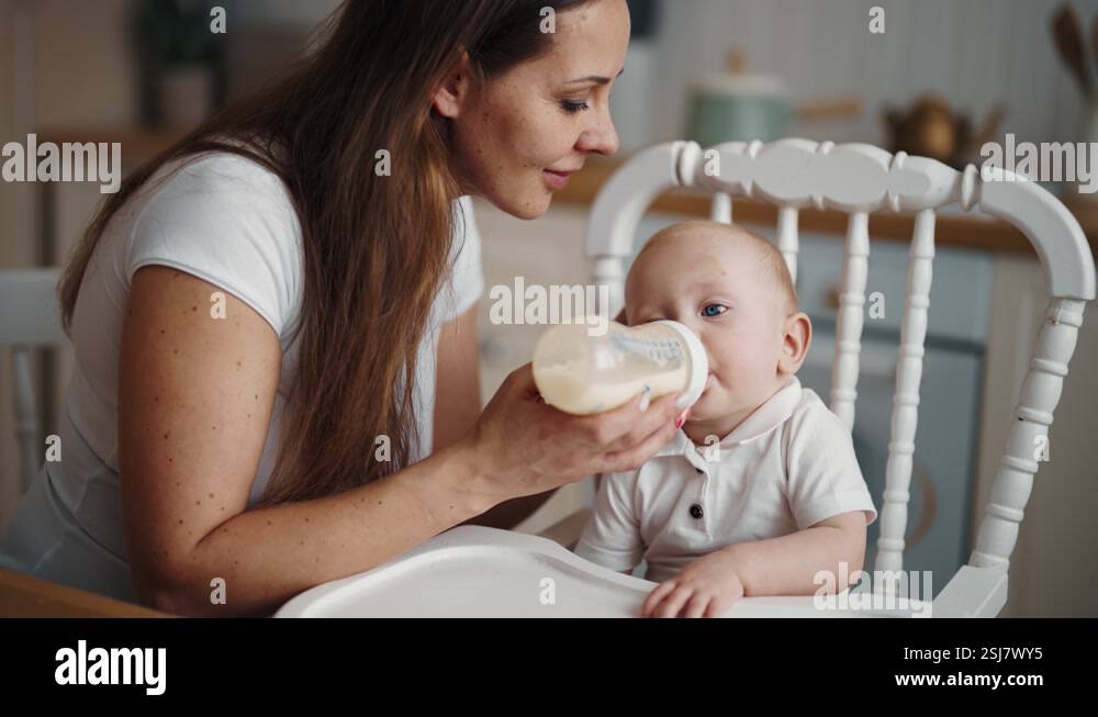 Mom feeding baby using bottle with milk mix kissing son to head. Mother ...