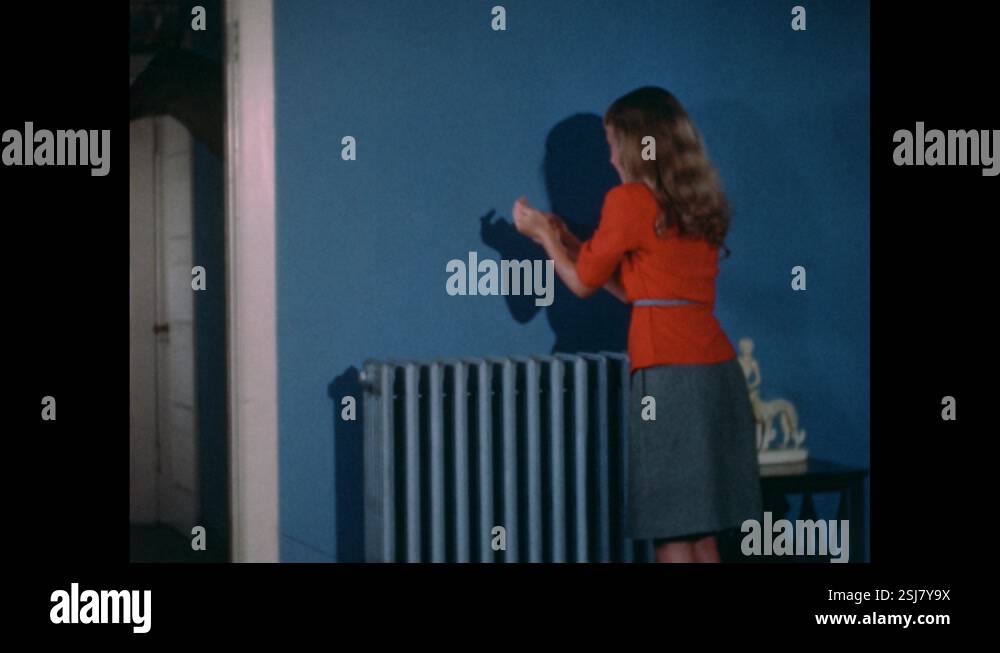 1950s: Teen girl puts her hand over radiator and opens hand. Feather ...