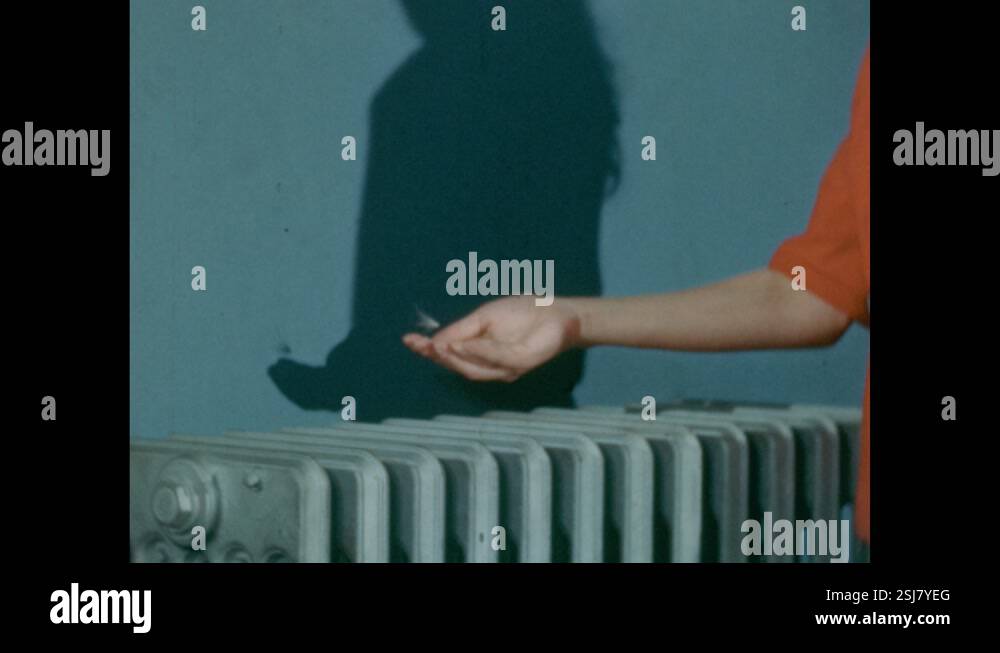 1950s: Teen girl puts her hand over radiator and opens hand. Feather ...
