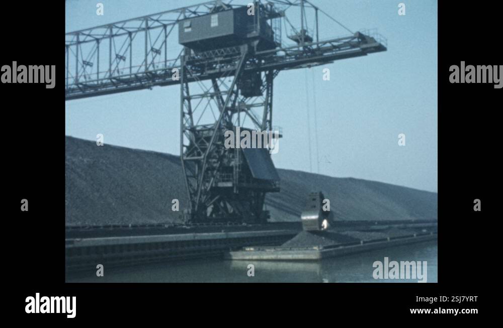 1950s: Coal barge is unloaded by a crane on the side of river Stock ...