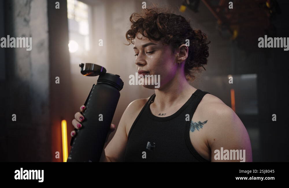 Attractive female weightlifter drinking water, relaxing and breathing ...