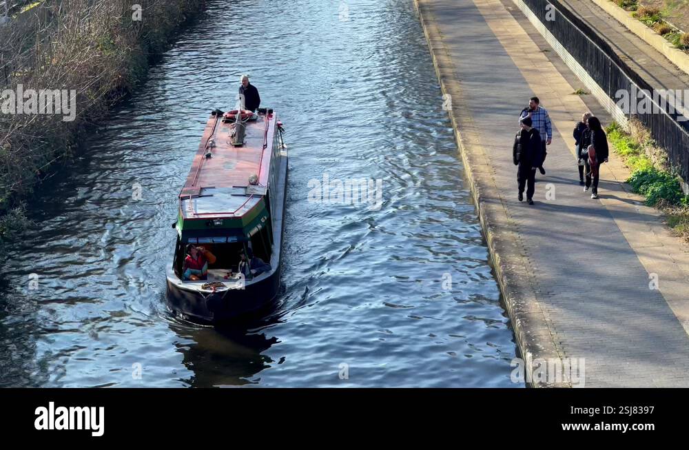Narrow boat cruising a river canal with some people walking by the ...