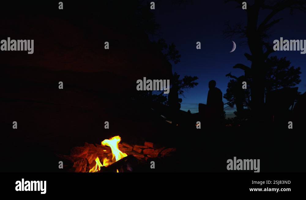 Orange campfire burns with blue hour silhouette people under moon Stock ...