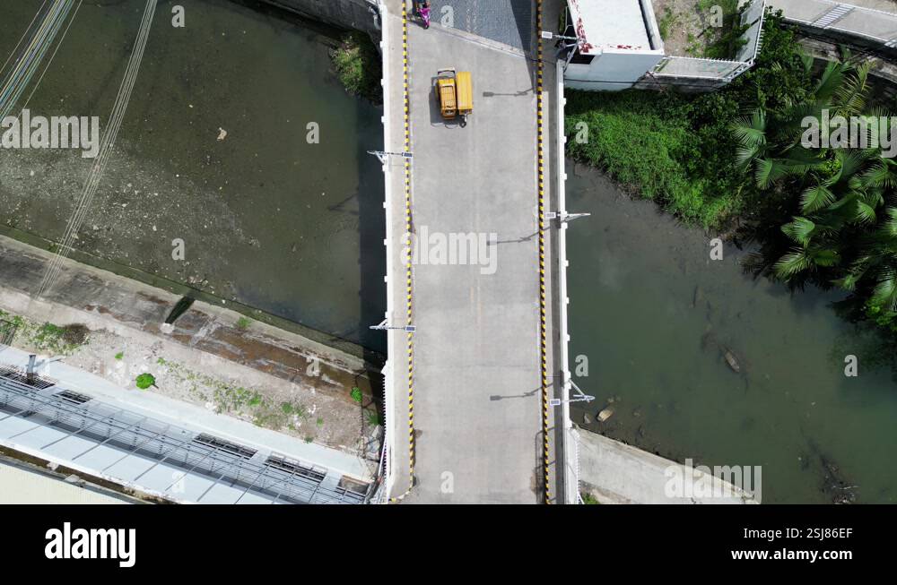 Aerial top down view along street with mopeds driving over bridge in ...