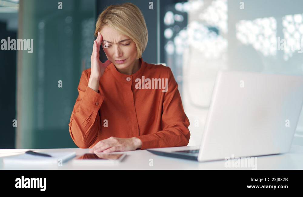 Sad young blonde woman suffering from headache while sitting at ...