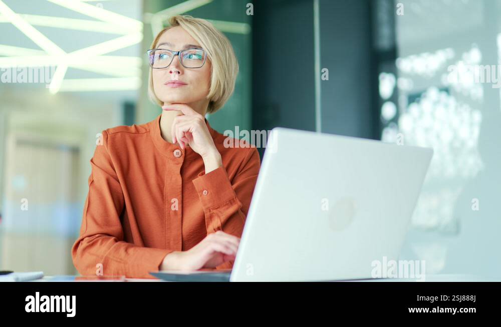 Thoughtful concentrated young female employee working on laptop while ...