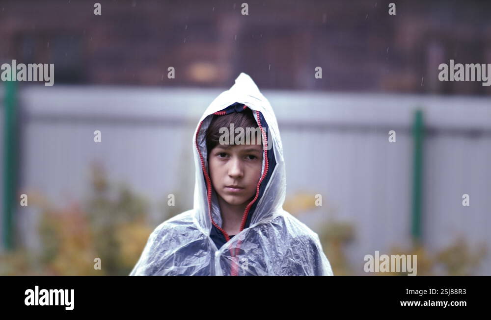 Sad boy standing in the rain with a raincoat, expressing pain on his ...