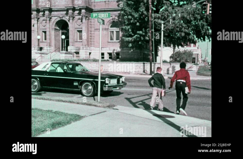 1970s: Boys on street corner at intersection. Car stops. Boys cross ...
