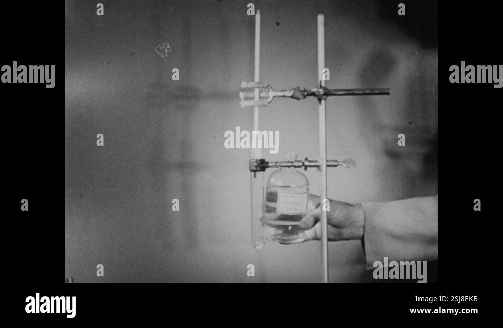 1950s: Lab equipment, hand pours liquid in test tube, puts burner under ...