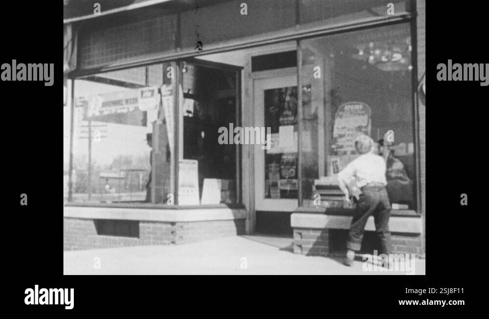 1950s: Boy looks into shop windows. Shop owner walks up and talks to ...