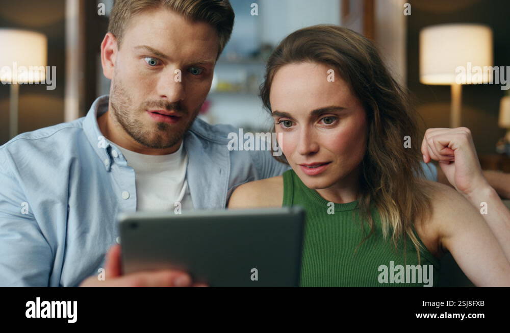 Surprised pair staring tablet home zoom on. Shocked spouses faces ...