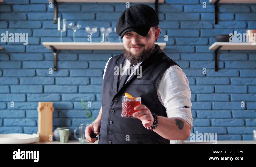 Cheerful positive handsome bartender with a tattoo and cap holds a ...