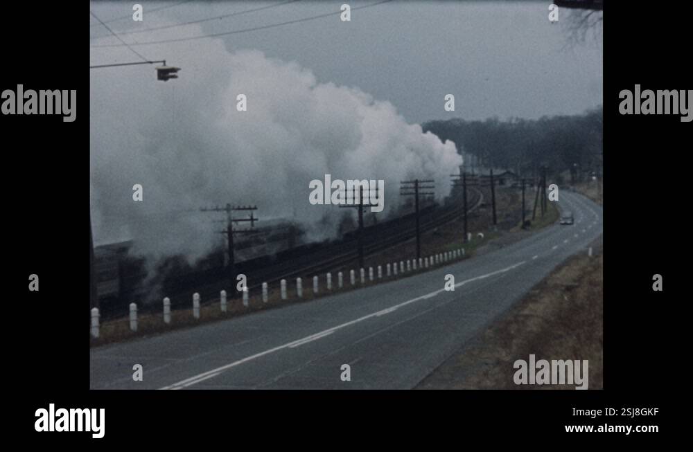1950s: Steam billows from train on railroad tracks near highway. Cars ...